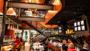 Um restaurante com interior moderno, apresentando uma escadaria, várias áreas de refeição e um bar.