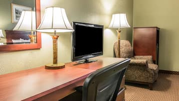 Quarto de hotel com escrivaninha de madeira, duas luminárias, uma televisão, poltrona estampada e um armário.