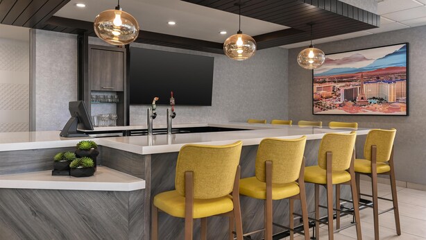 Cozinha moderna com ilha central, banquetas, iluminação pendente, televisão de tela plana e uma grande pintura de paisagem urbana.