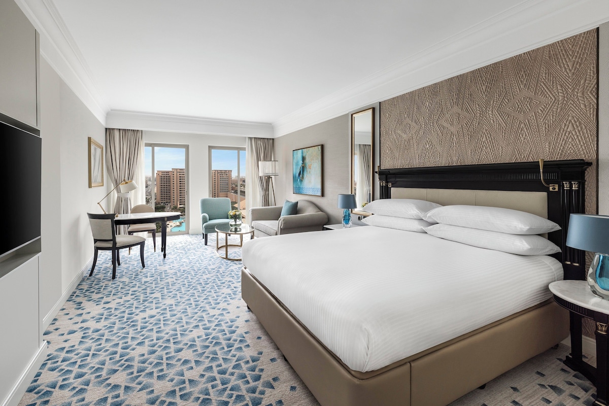 Quarto de hotel com uma cama grande, escrivaninha, cadeira e vista da cidade.