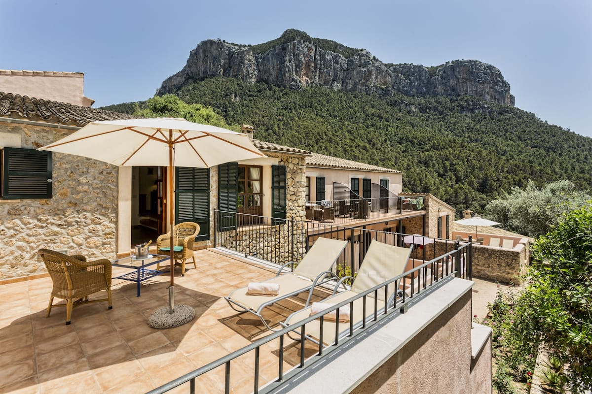 Terraço com cadeiras de estar e mesa, com vista para uma paisagem montanhosa.
