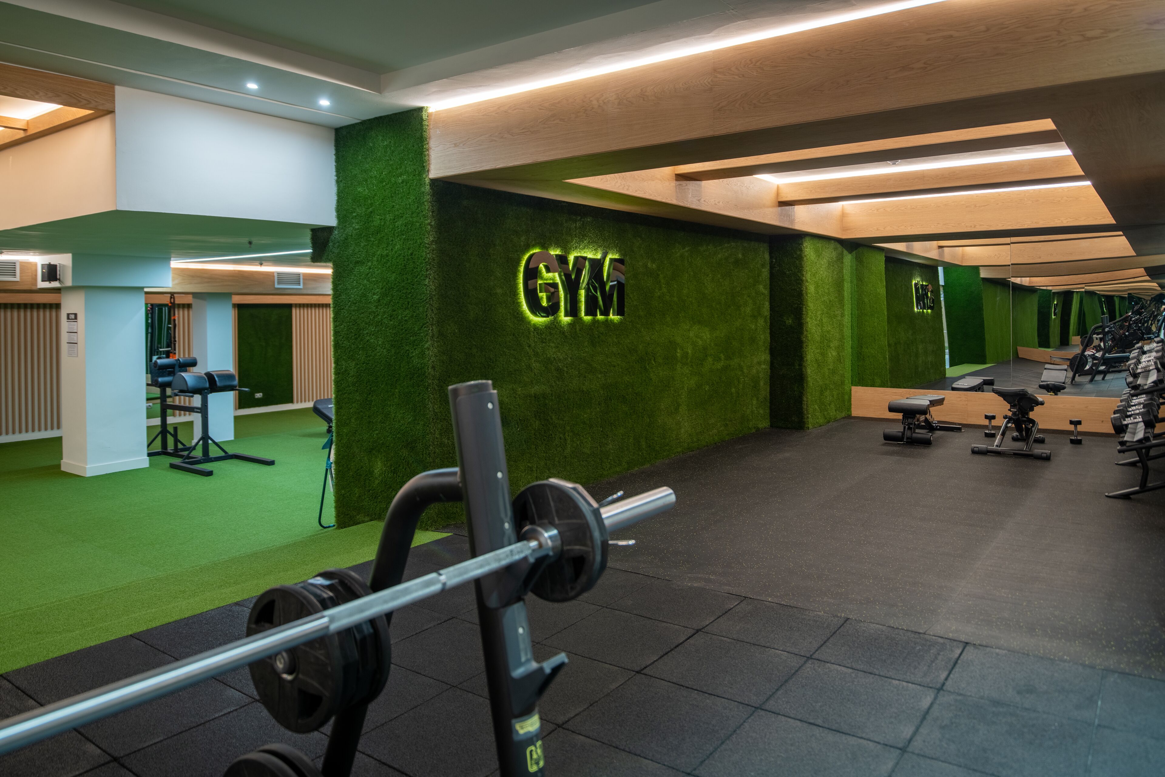 Academia moderna com paredes verdes, área de musculação visível e espelho refletindo o espaço.