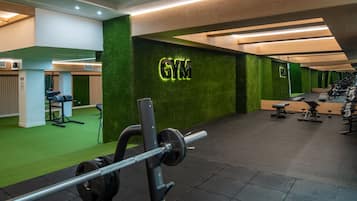 Academia moderna com paredes verdes, área de musculação visível e espelho refletindo o espaço.