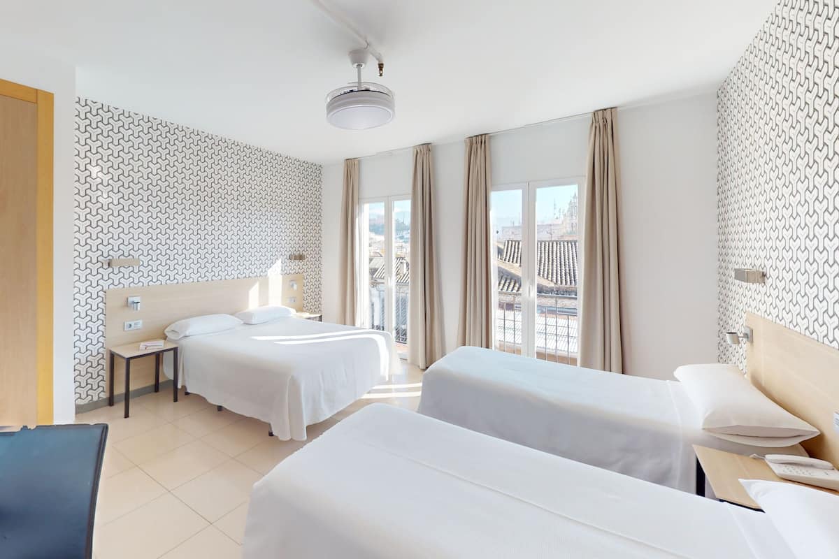 Quarto de hotel com duas camas, uma escrivaninha, um guarda-roupa e varanda com vista para a cidade.