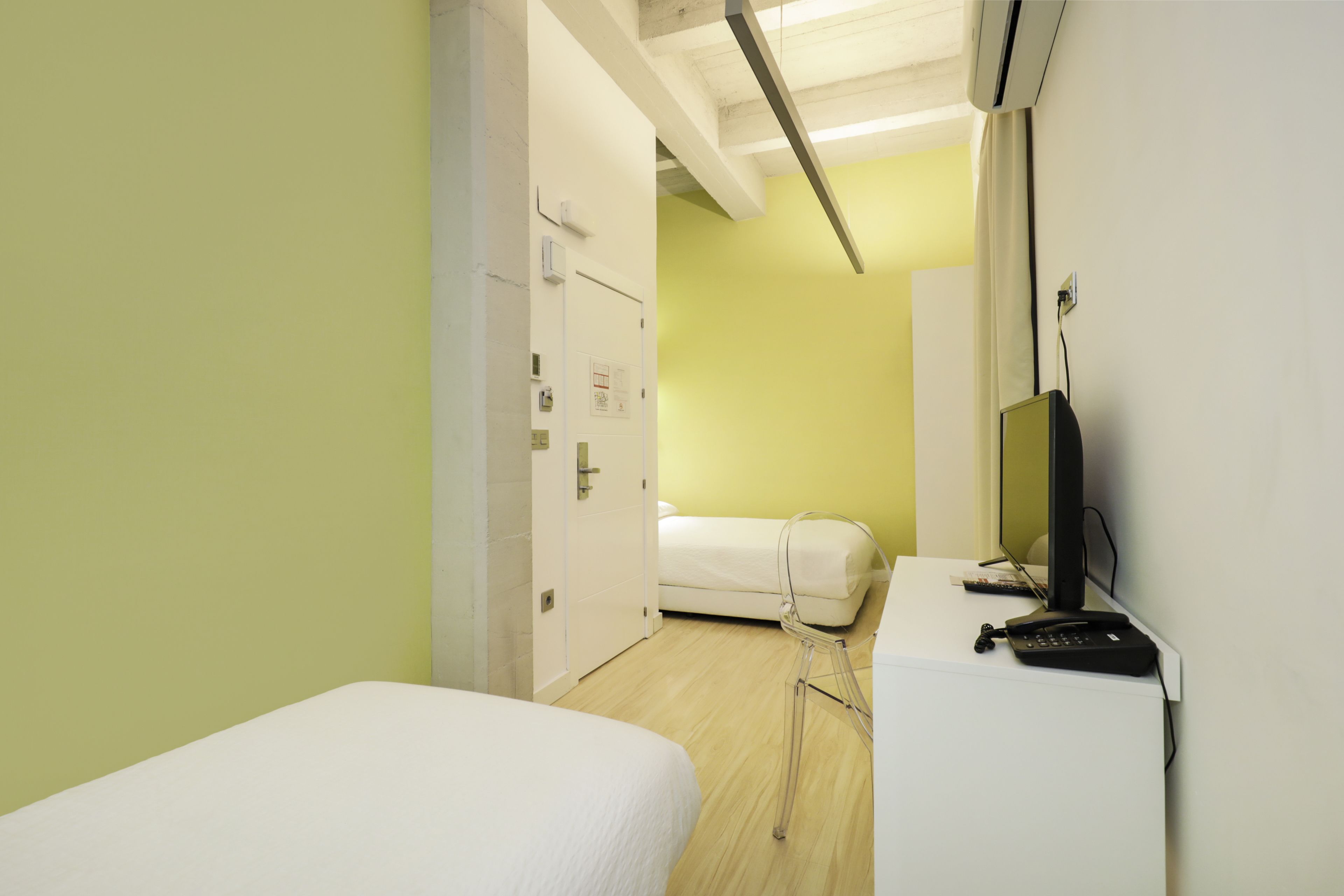 Quarto de hotel com uma cama, uma escrivaninha com computador e uma cadeira.