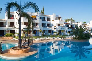 Resort com piscina, palmeiras e edifícios brancos com varandas.