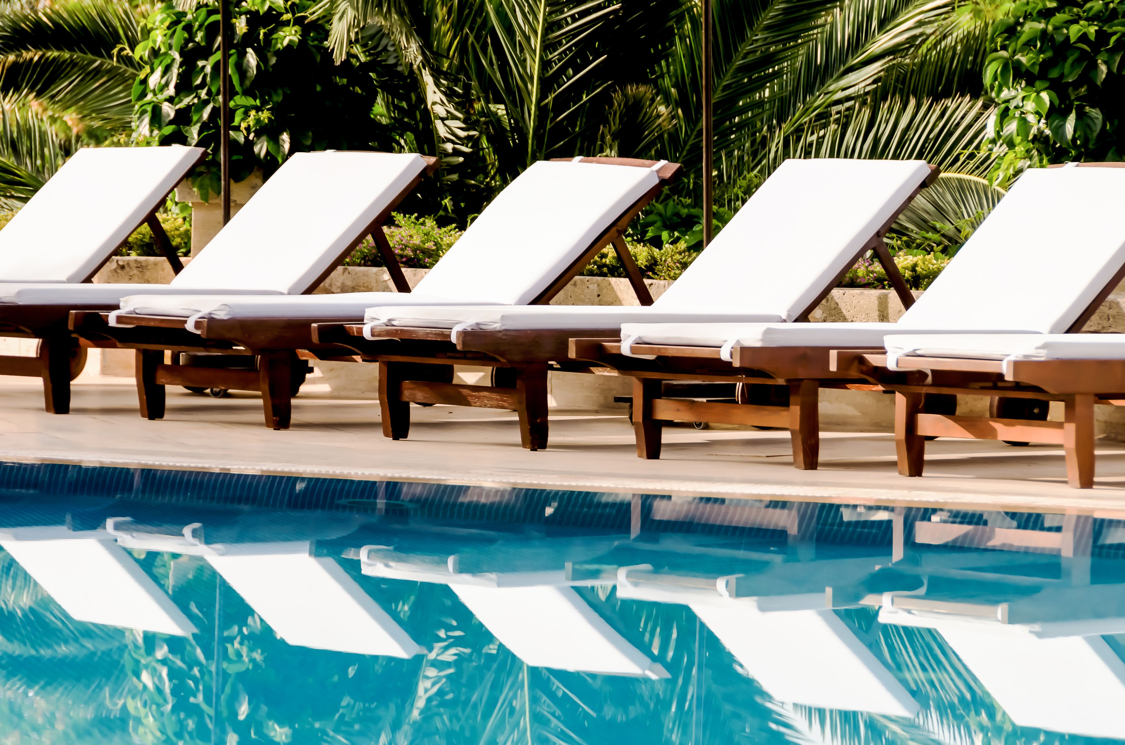 Área ao lado da piscina com espreguiçadeiras e uma piscina azul cristalina.