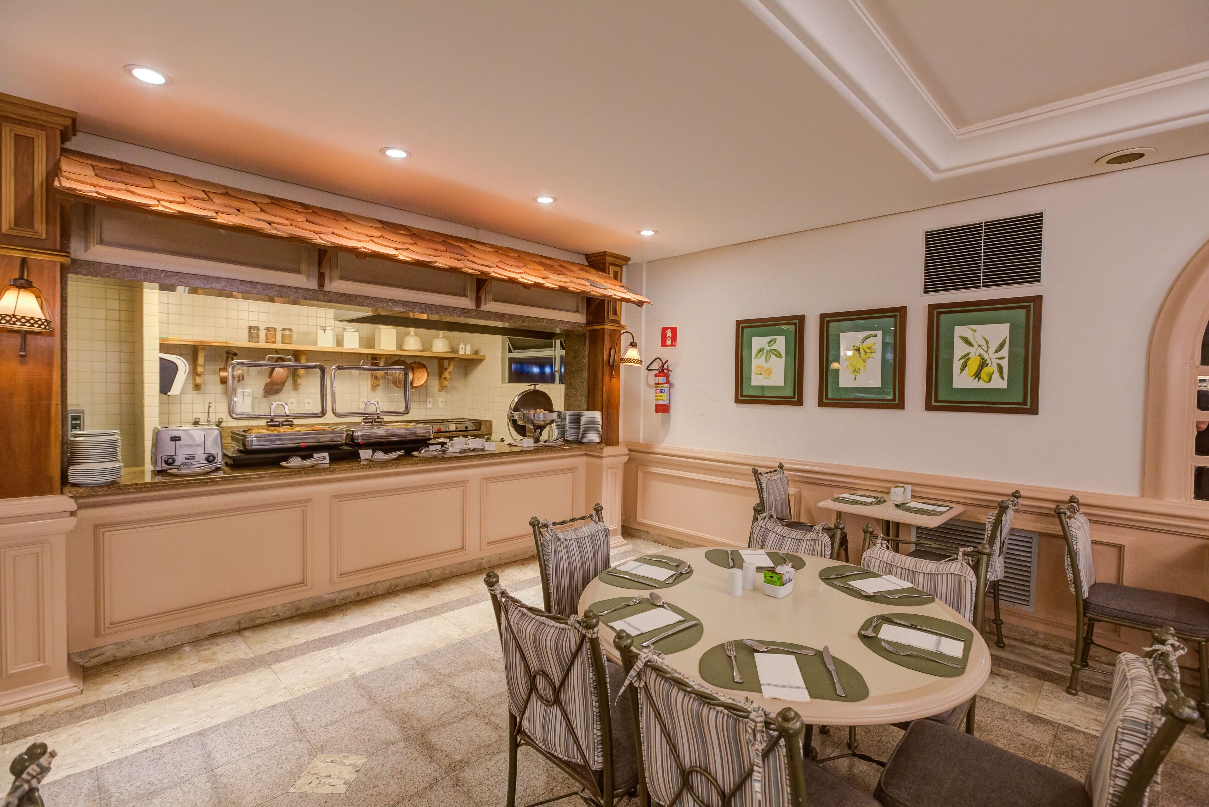 Uma área de refeições com serviço de buffet, uma mesa redonda com cadeiras e quadros nas paredes.