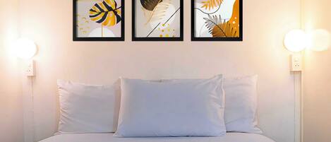 Uma cama com roupa de cama branca, um cobertor amarelo estampado e três quadros emoldurados acima.