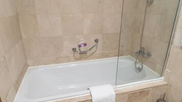 Um banheiro moderno com banheira, box de vidro e dispensador de álcool em gel na parede.