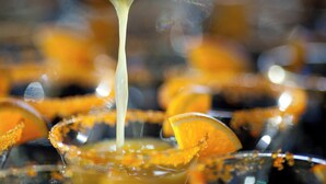 Close-up de uma bebida sendo servida em um copo com borda salgada, rodeado de rodelas de laranja.