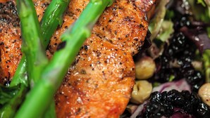 Close-up de um filé de salmão cozido com aspargos e uma salada mista de folhas verdes.