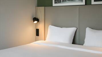 Uma cama bem arrumada com lençóis brancos, um luminária fixada na parede e um quadro emoldurado acima da cama.