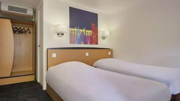 Quarto de hotel com duas camas, um guarda-roupa, ar-condicionado fixado na parede e uma pintura com vista para a cidade.
