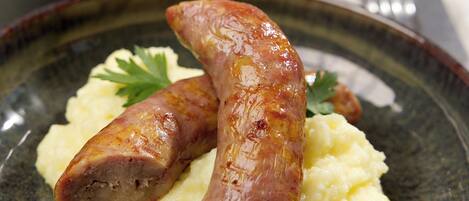 Um prato de salsichas e purê de batatas em um prato de cerâmica.
