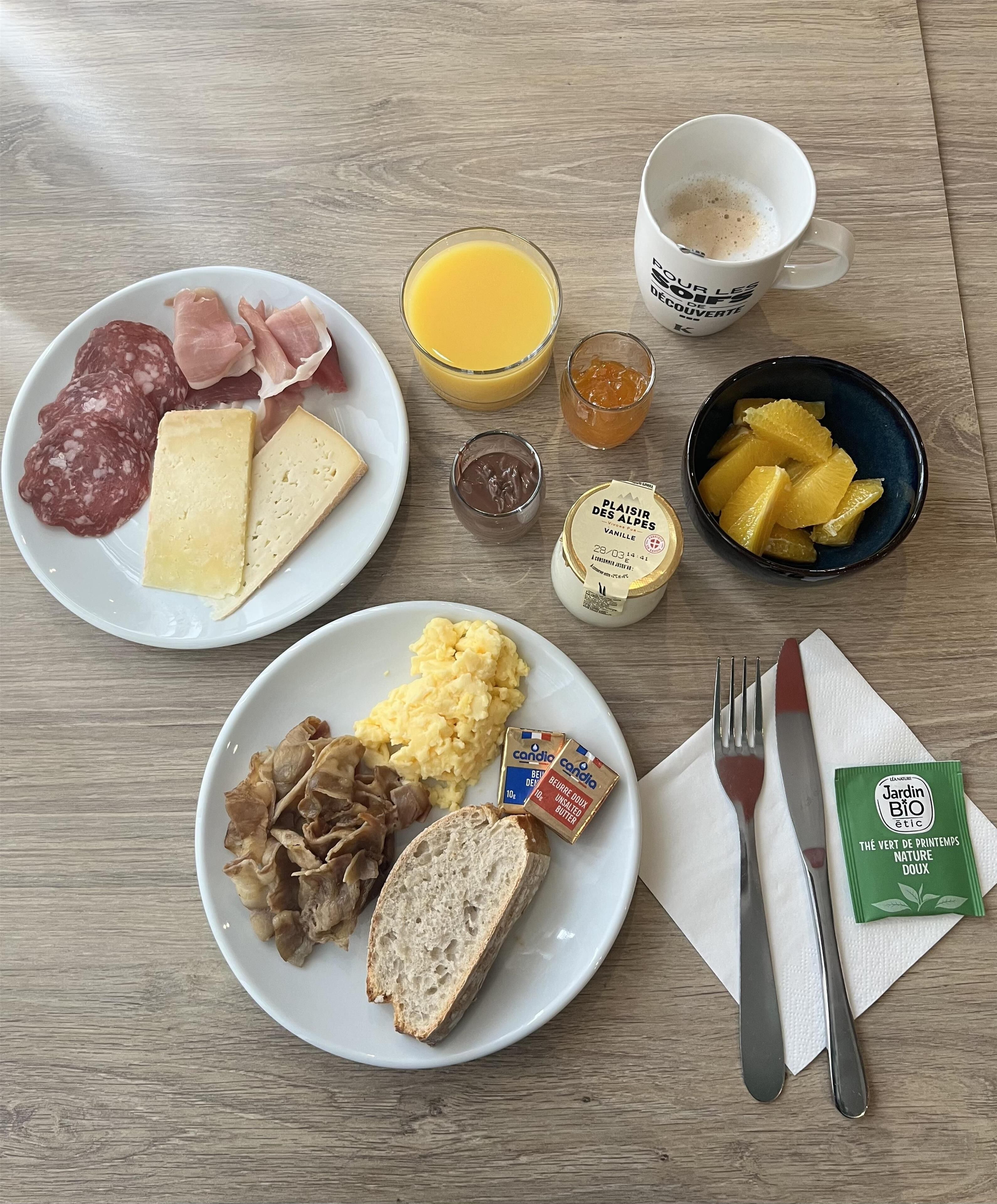 Mesa de madeira com pratos de comida, uma xícara de café e garfo e faca.
