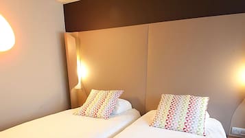 Quarto de hotel com cama, duas almofadas, luminária na parede e tomada.