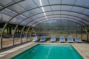 Uma piscina coberta com espreguiçadeiras e um compartimento de vidro.
