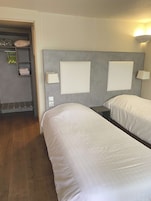 Quarto de hotel com duas camas, um guarda-roupa e uma mesa de cabeceira com luminárias.