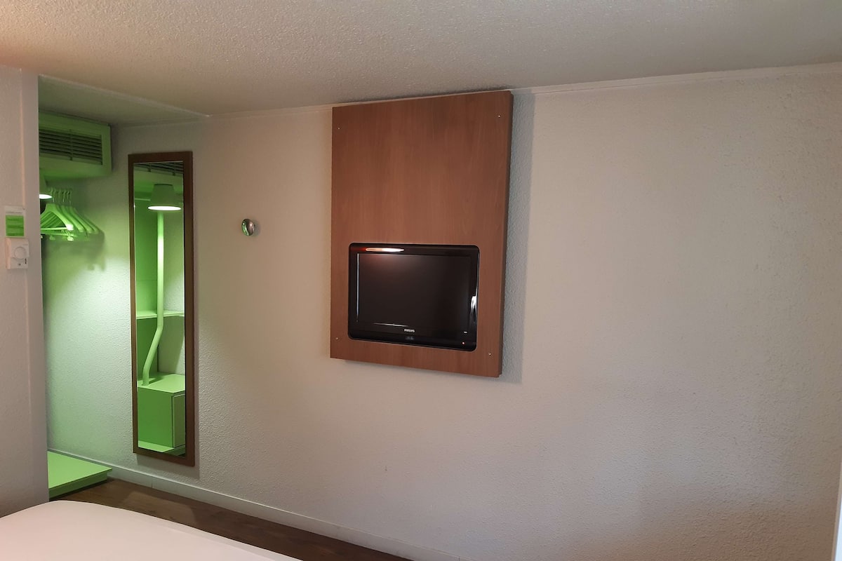 Quarto de hotel com cama, televisão na parede e espelho.