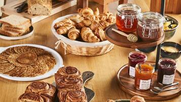 Diversos pães e doces em uma mesa de madeira, incluindo croissants, baguetes e uma barra de pão.