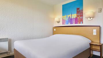 Quarto de hotel com uma cama grande, um quadro na parede, duas luminárias de cabeceira e uma pequena mesa de cabeceira de madeira.