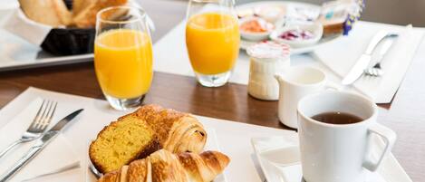 Uma mesa posta para o café da manhã, com croissants, suco de laranja e café.