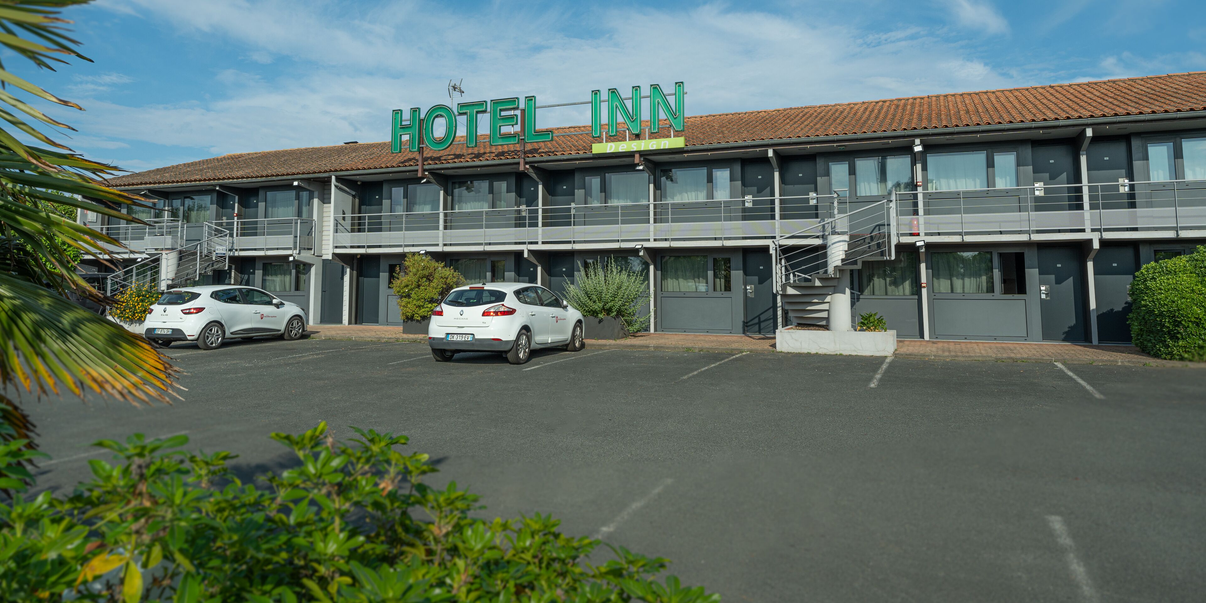Um hotel com design moderno, apresentando um estacionamento com dois carros e uma placa que diz "HOTEL INN".