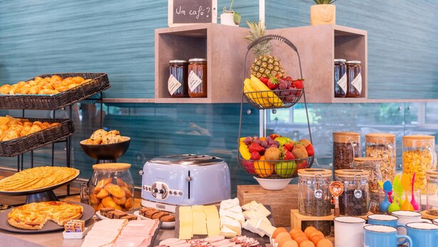 Um buffet de café da manhã com diversos alimentos, incluindo pães, frutas, queijos e frios.