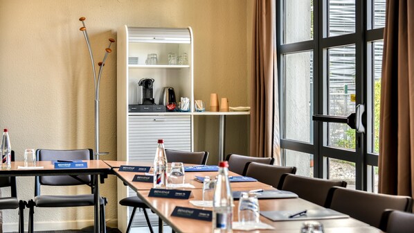 Uma sala de conferências com uma mesa comprida, cartões de nome, garrafas de água e uma máquina de café.