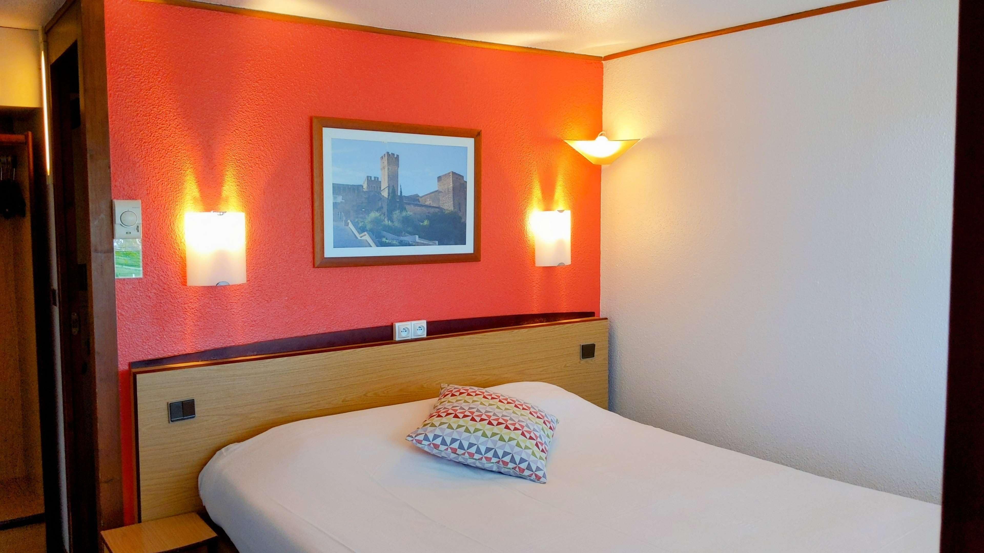 Quarto de hotel com cama, quadro pendurado na parede e duas luminárias.