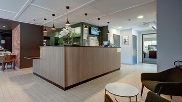 Uma área de recepção com balcão de madeira, televisão e um espaço de estar com uma mesa redonda e cadeiras.