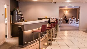 Uma área de bar com balcão, banquetas vermelhas e um espaço de estar com cadeiras brancas.