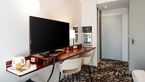 Quarto de hotel com televisão, escrivaninha, cadeira, mesa pequena com chaleira, xícara e bandeja com lanches.