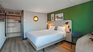 Quarto de hotel moderno com cama, abajures, escrivaninha e uma cadeira.