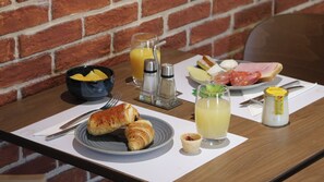 Mesa de café da manhã com croissants, um copo de suco e um prato de presunto e queijo.