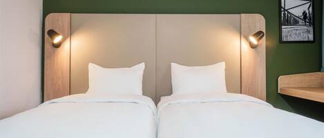 Cama de casal com duas almofadas, cabeceira de madeira e luminárias de leitura fixadas na parede.