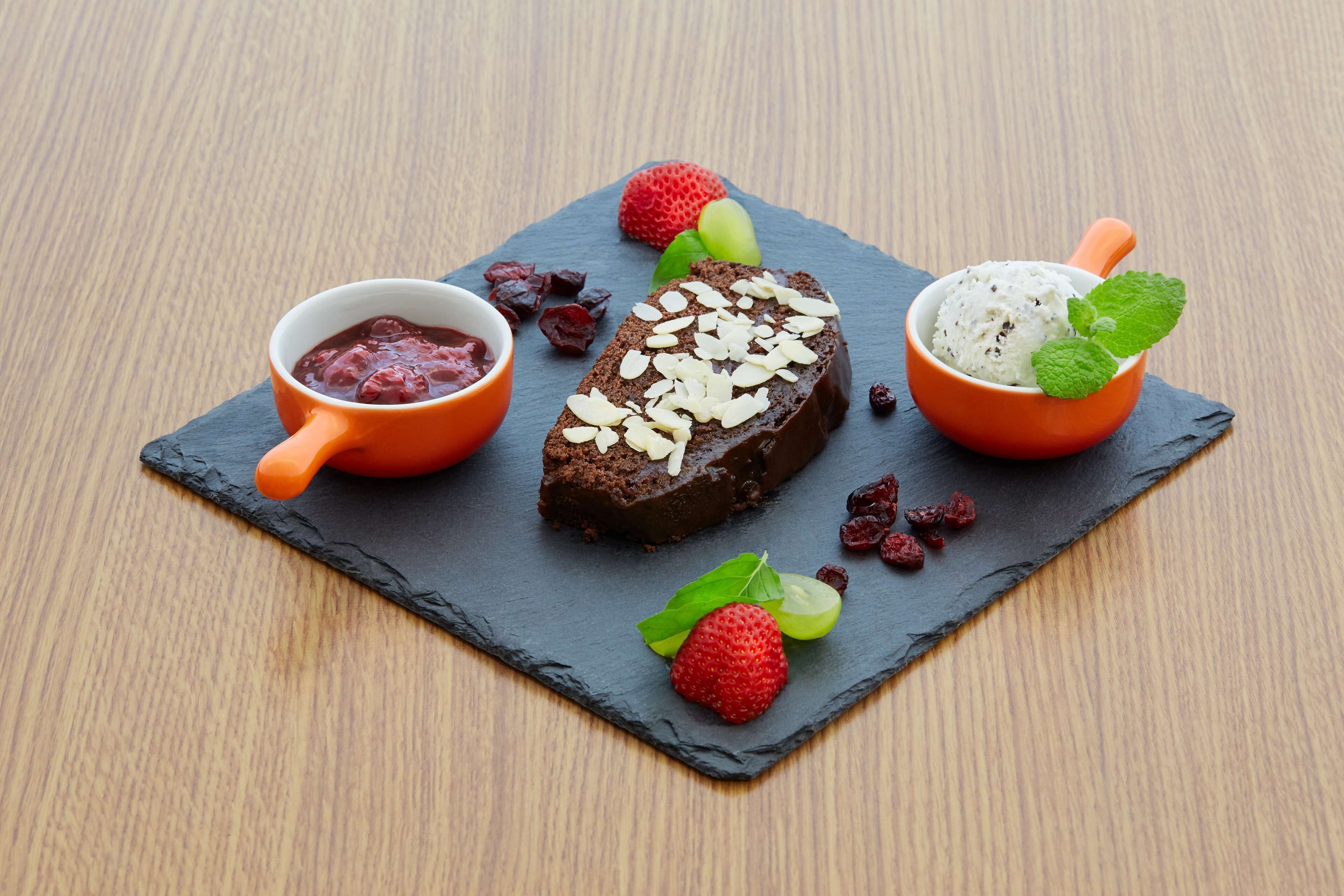 Um prato de sobremesa com bolo de chocolate, morangos e duas taças de sorvete sobre uma lousa.