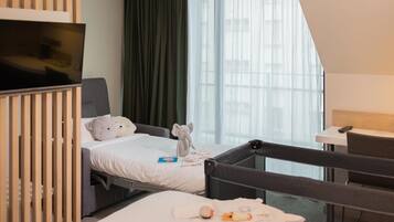 Quarto de hotel com cama, cadeira, televisão e janela com cortinas.