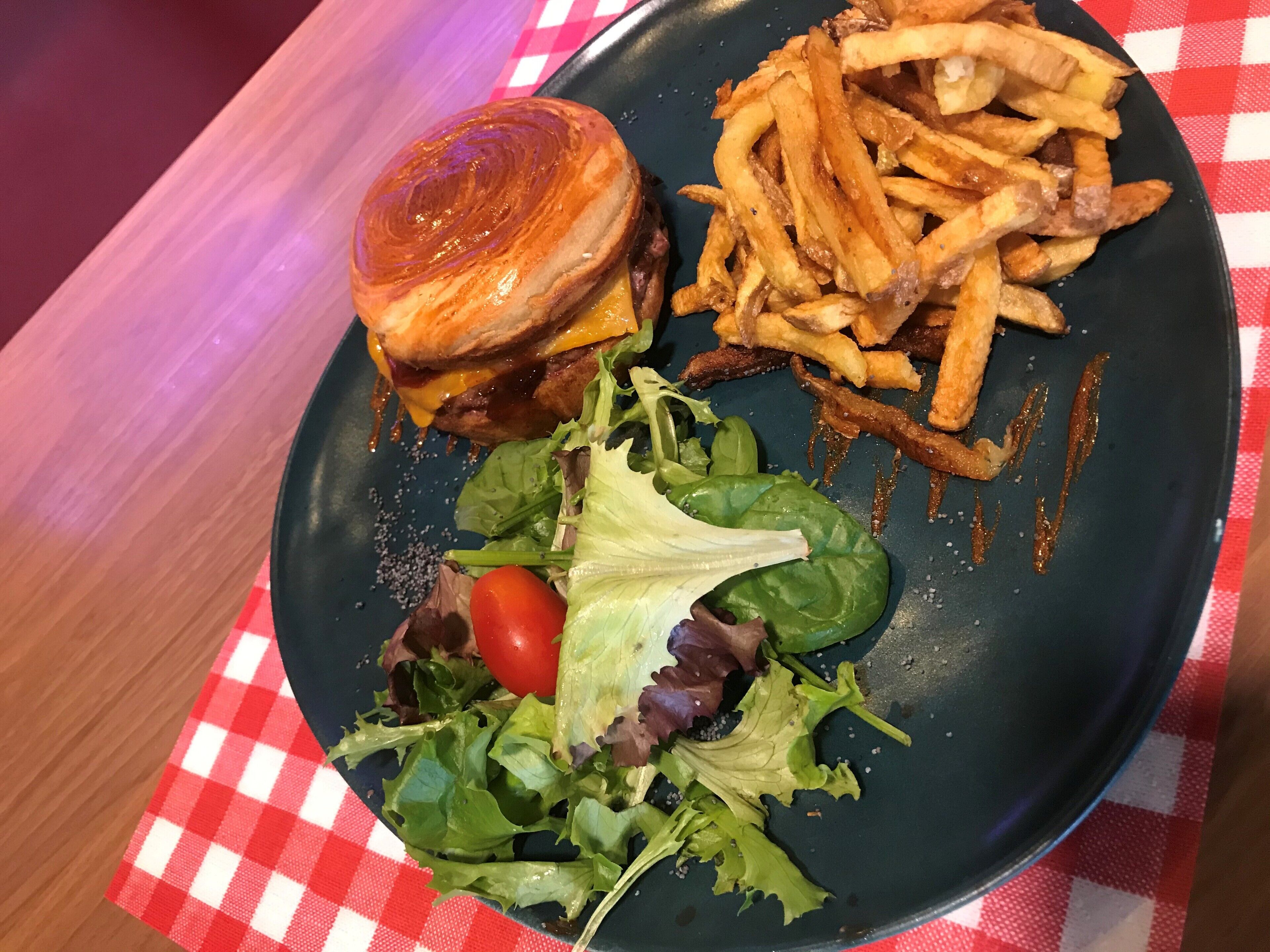 Um prato com hambúrguer, batatas fritas e uma salada acompanhamento sobre uma mesa com toalha xadrez vermelha e branca.