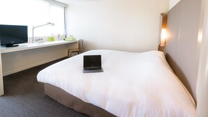 Quarto de hotel com cama, escrivaninha com laptop, televisão e janela com persianas.