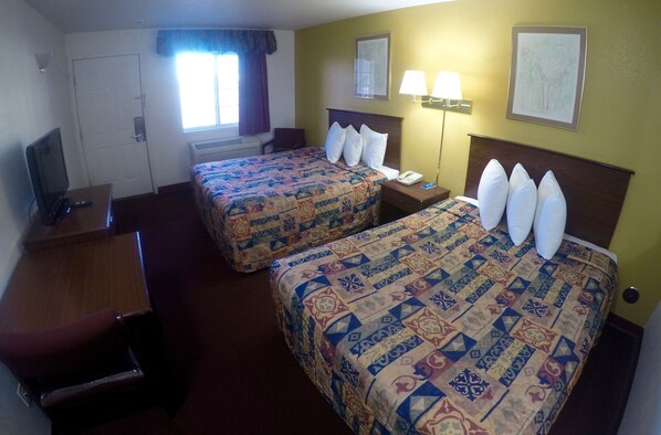 Quarto de hotel com duas camas, uma escrivaninha, televisão e janela com cortinas.