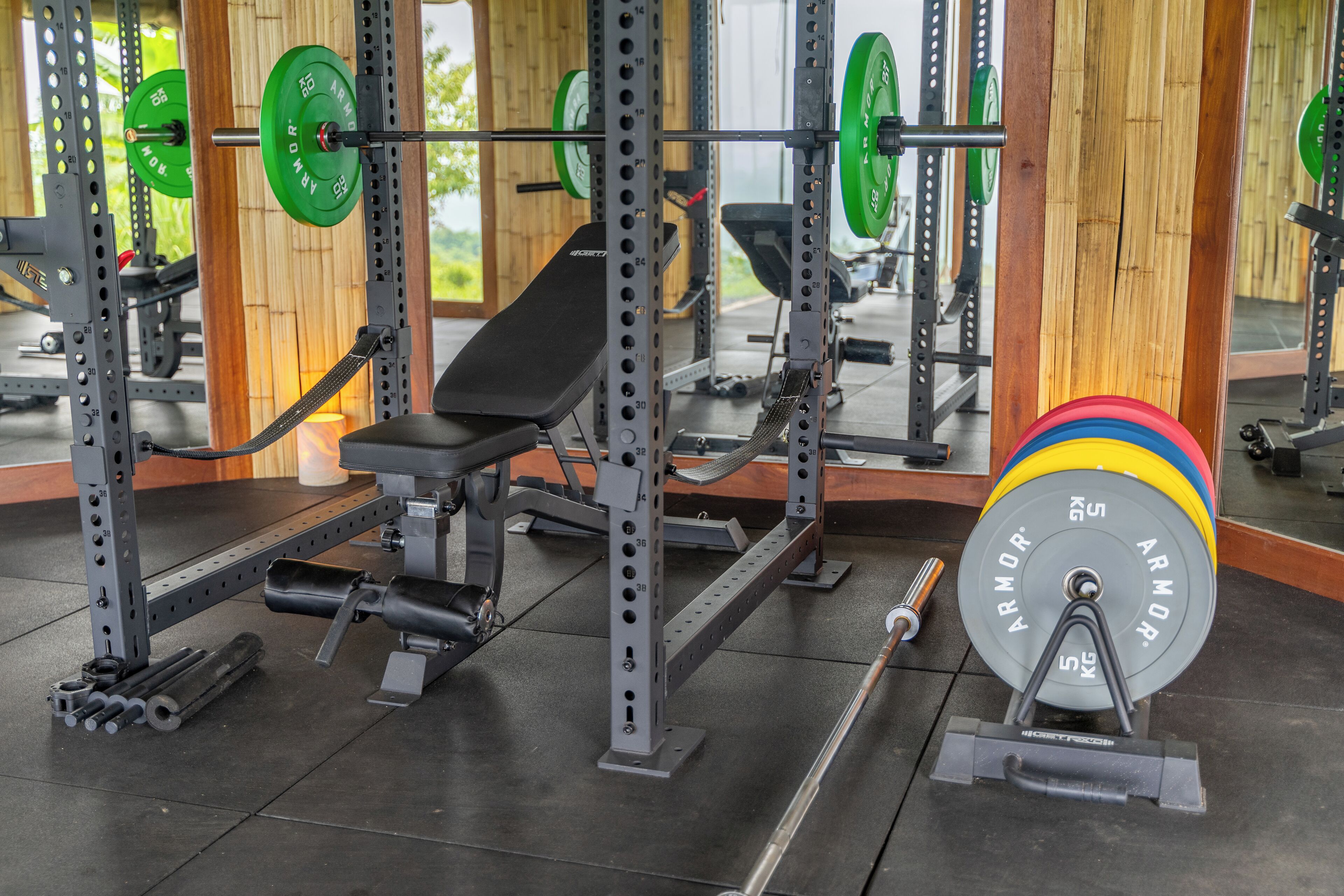 Uma academia com equipamentos de musculação, bancos e um espelho refletindo o espaço.