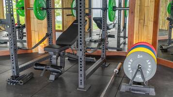 Uma academia com equipamentos de musculação, bancos e um espelho refletindo o espaço.