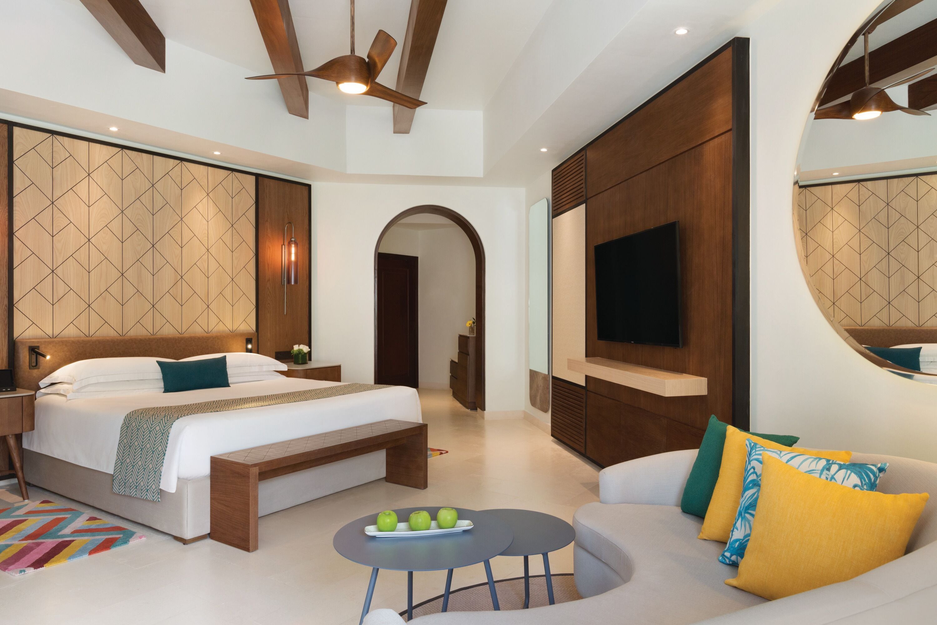 Quarto de hotel moderno com uma cama grande, um sofá, uma mesa de centro e uma televisão.