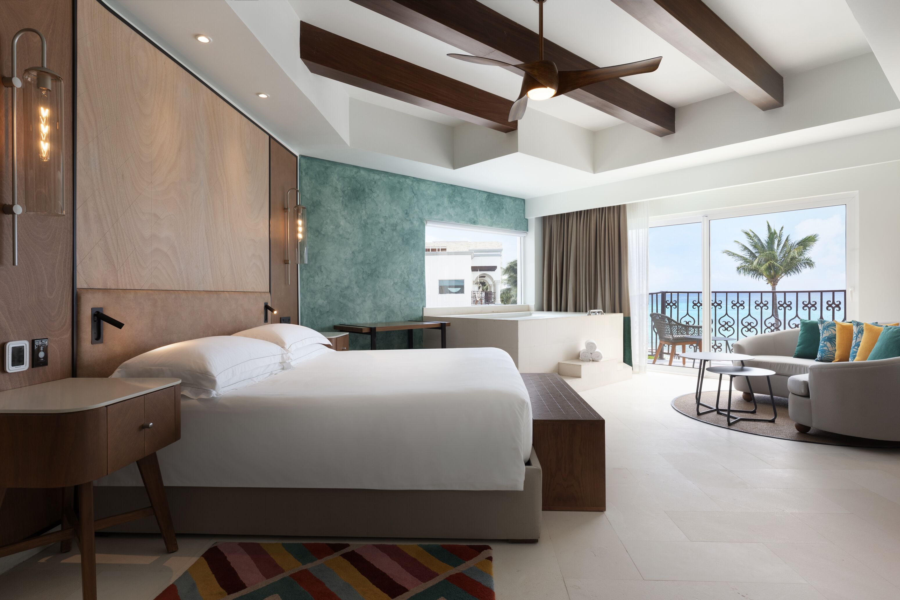 Quarto de hotel moderno com uma cama grande, uma escrivaninha, varanda com vista e um ventilador de teto.
