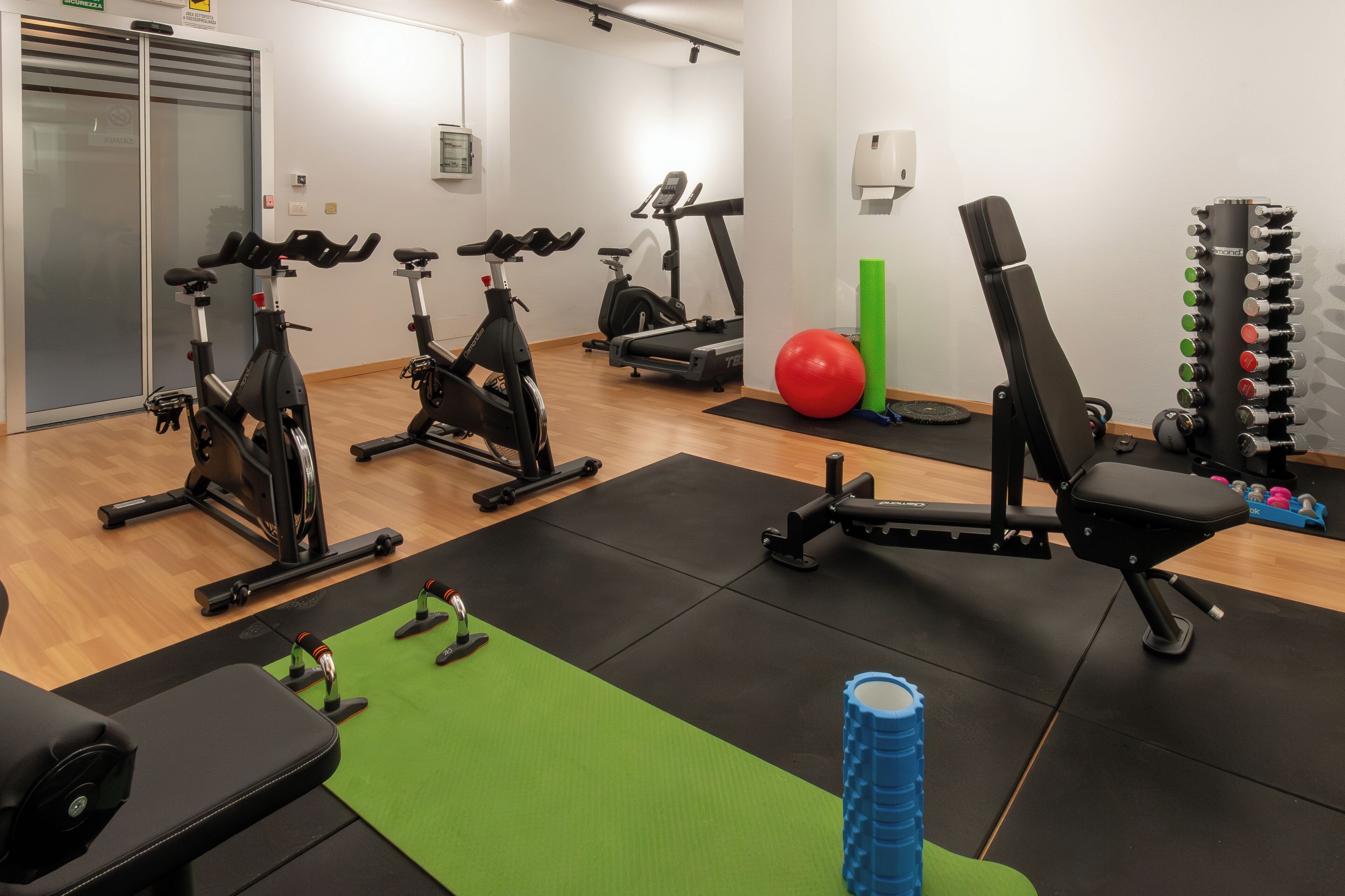Uma academia com bicicletas ergométricas, elíptica, um banco e torre de pesos.
