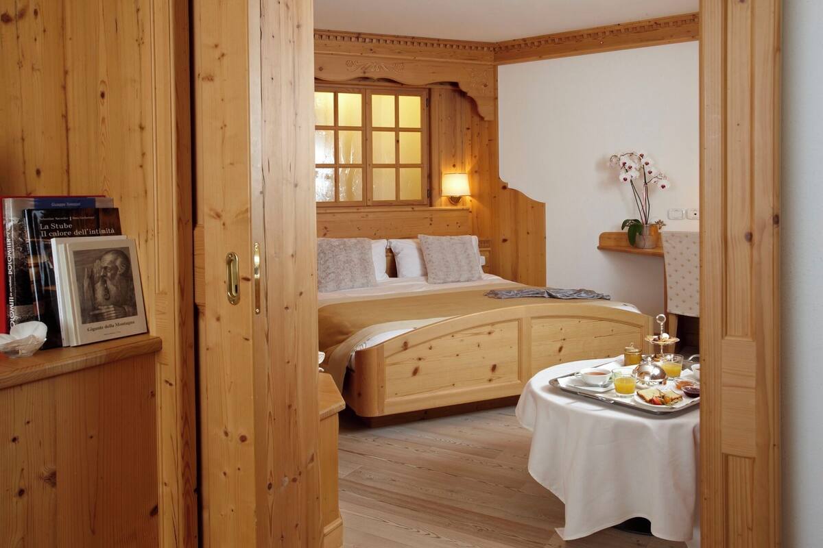 Quarto de madeira com cama, mesa com café da manhã e janela com cortinas.