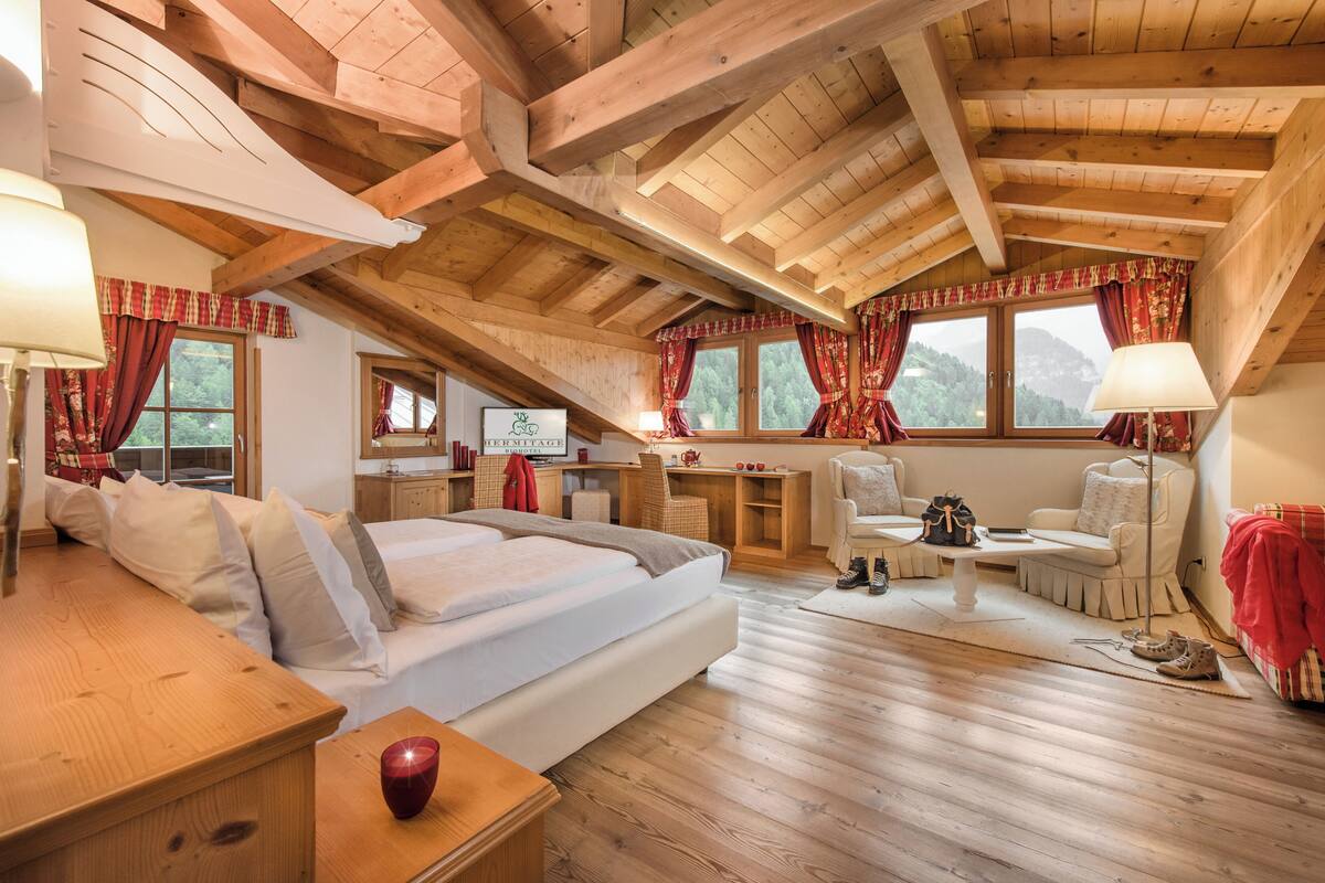 Um quarto de sótão acolhedor com teto de madeira, uma cama grande, uma escrivaninha e uma cadeira.