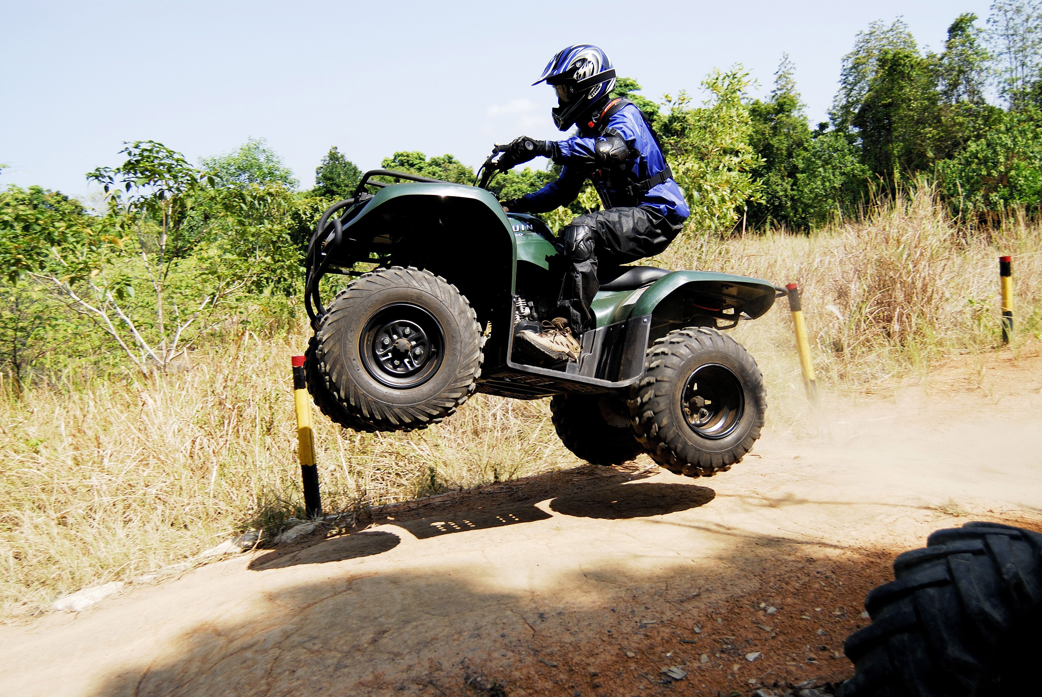 Uma pessoa conduz uma moto de trilha por um caminho de terra, rodeada por vegetação.